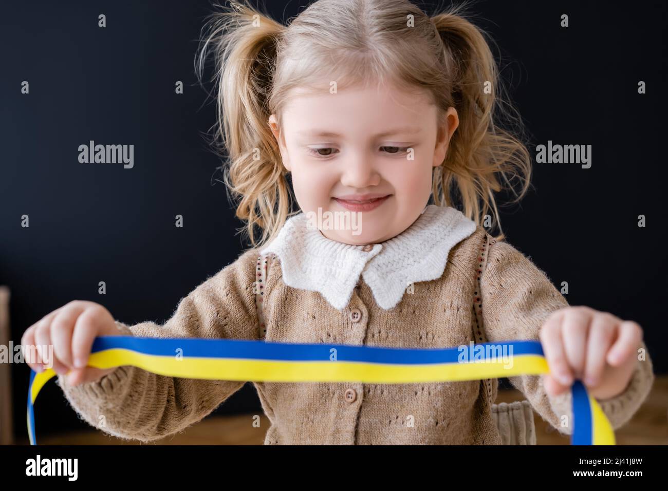 happy girl with ponytails holding blue and yellow ribbon on black Stock ...
