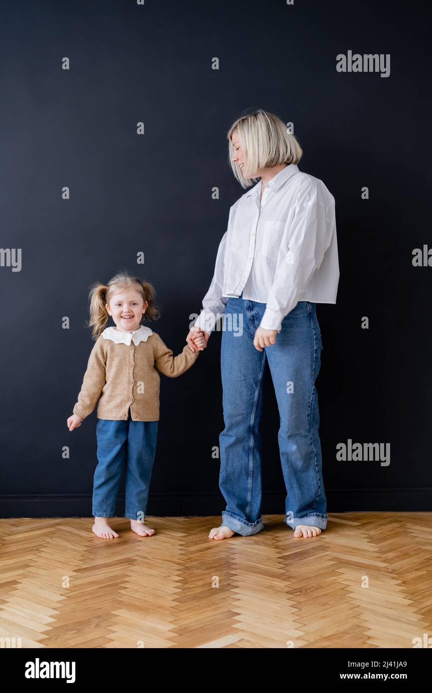 full length view of barefoot mother and daughter holding hands near ...