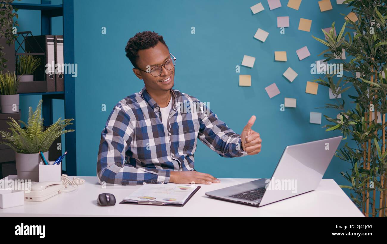 Positive employee giving thumbs up in front of laptop screen, showing ...