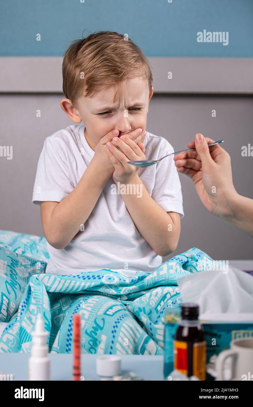 A sick boy covers his mouth with his hands when his mother tries to ...