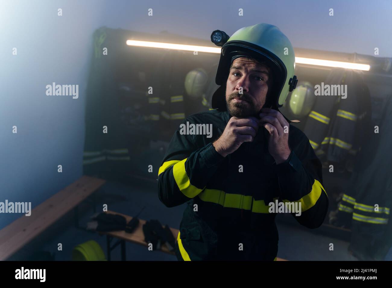 Mature firefighter preparing for action in fire station at night ...