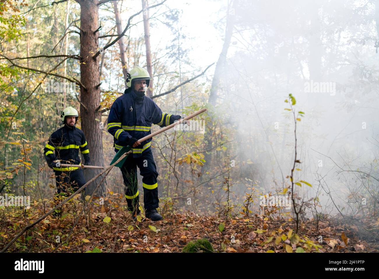 Firefighters men at action, running through smoke with shovels to stop ...