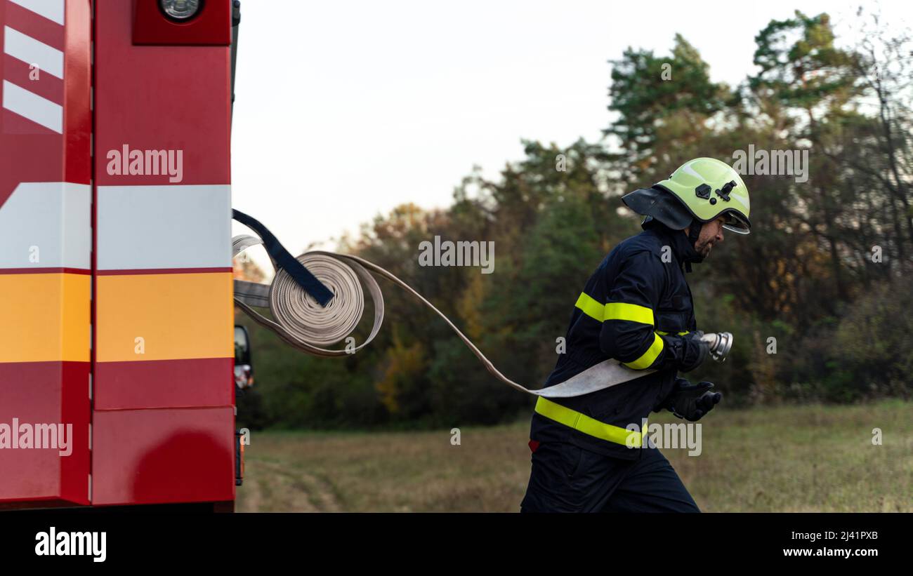 Firefighter at action taking hose from fire truck outdoors in nature ...