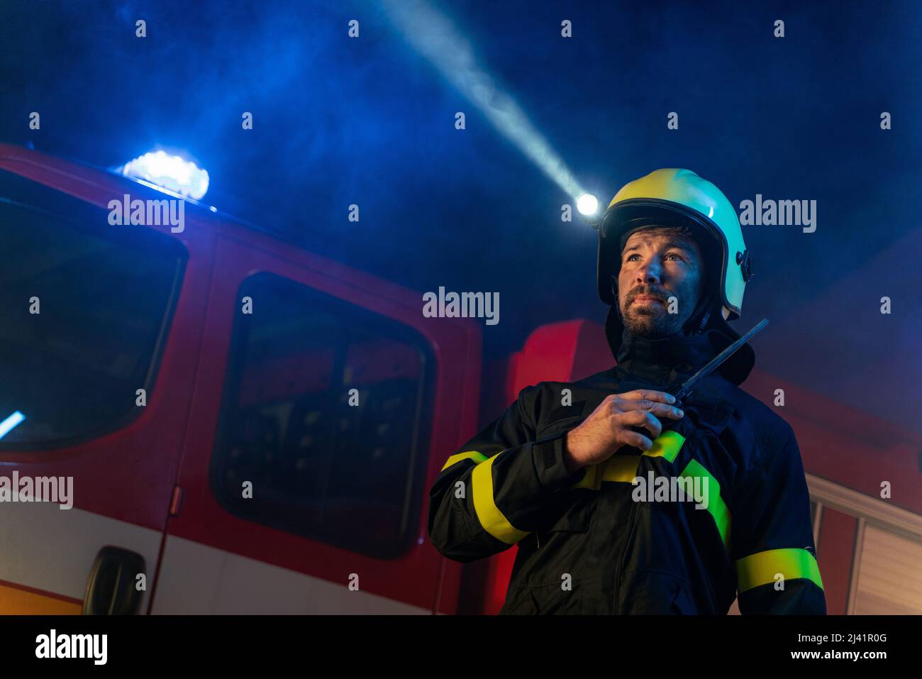 Low angle view of firefighter with fire truck in background at night ...
