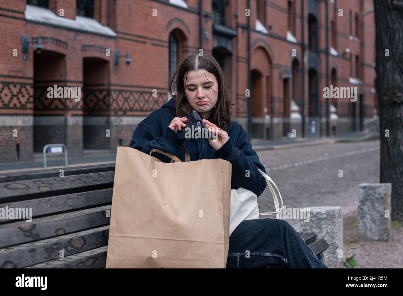 A young woman sits on a bench with an empty wallet, concept of lack of ...