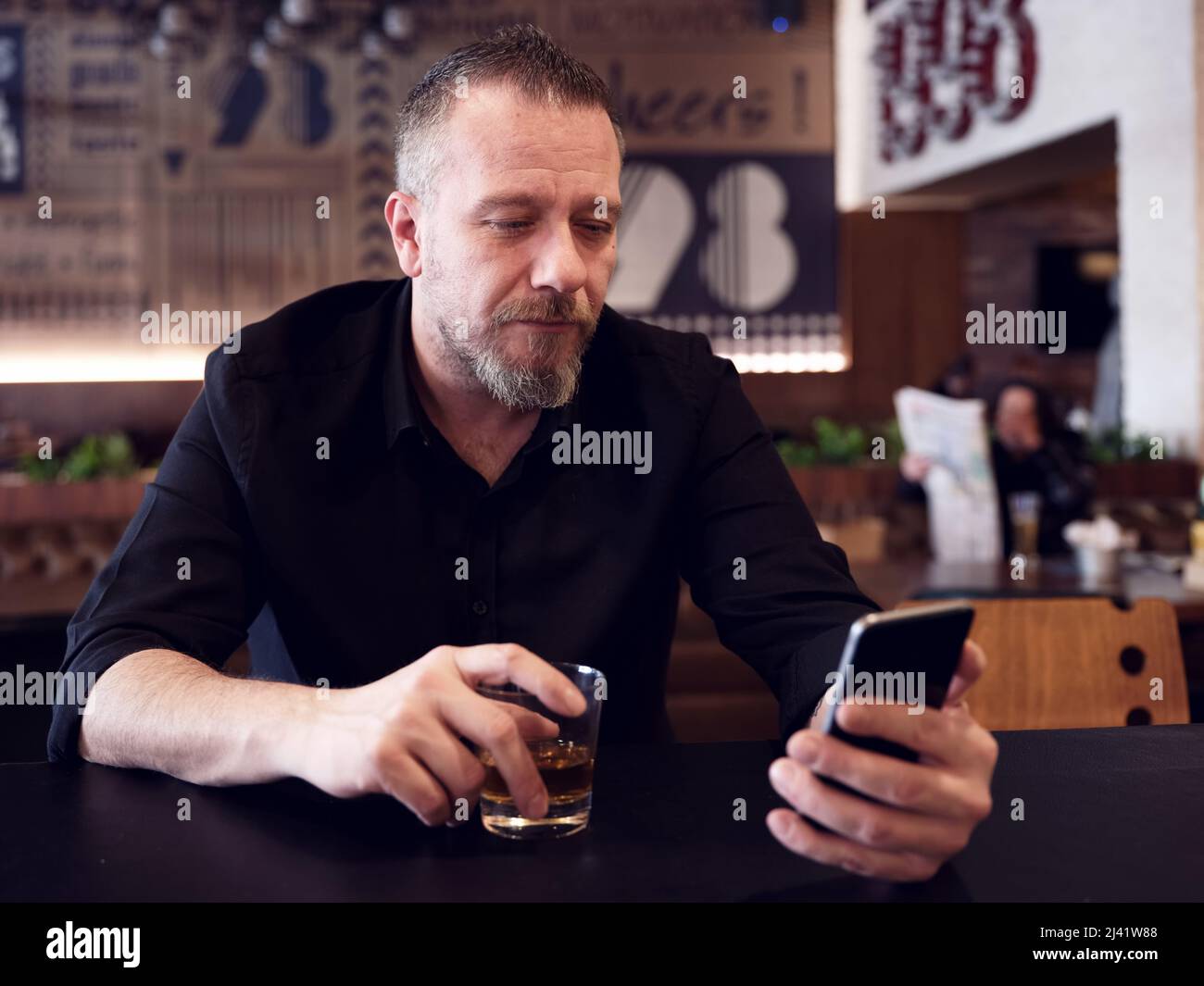 Caucasian middle age man holding a glass of whiskey sits at the bar ...