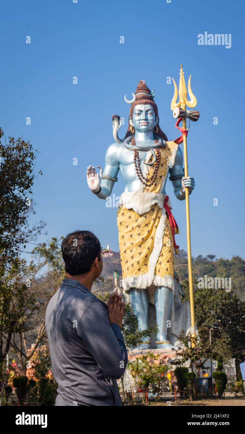young man doing pryer of shiva statue with bright blue sky background ...