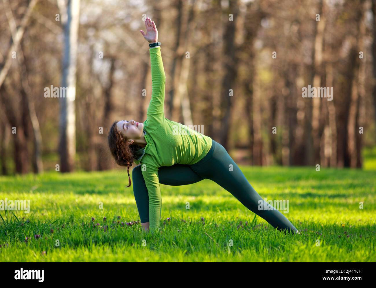 Young woman yogi in park on the green grass doing fitness exercises ...