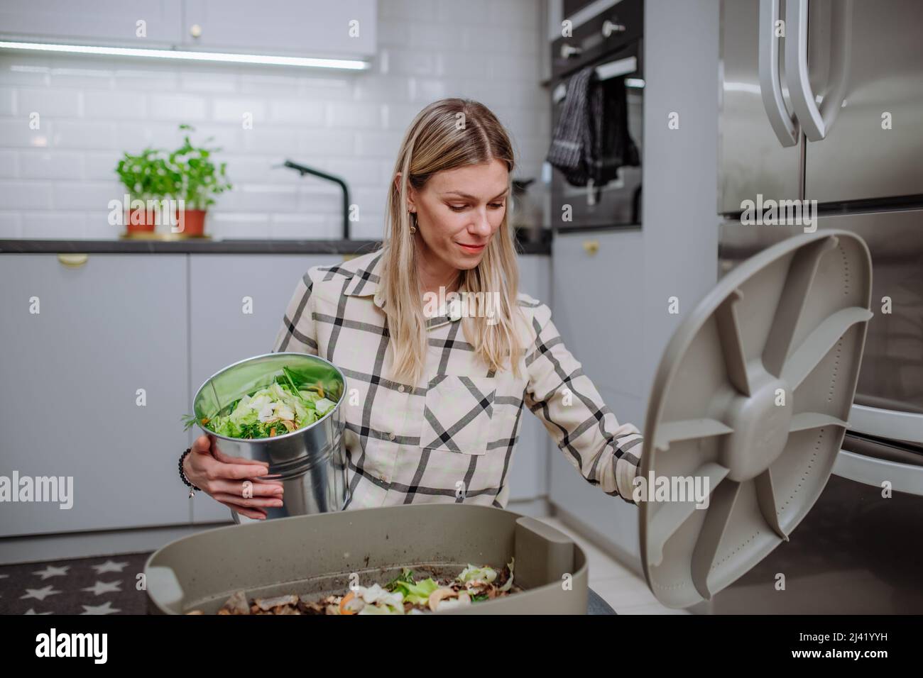 Woman throwing vegetable cuttings in a compost bucket in kitchen Stock ...