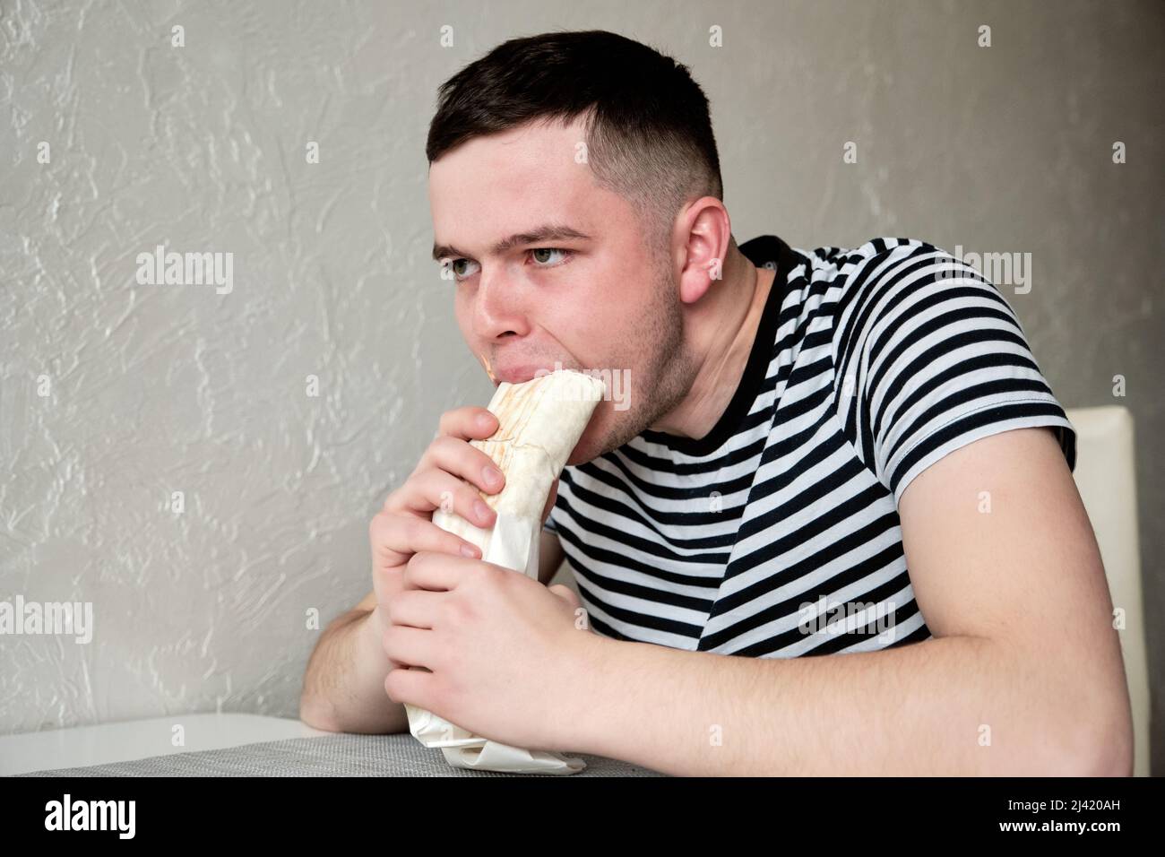 Handsome Young Man Eating Kebab. Hungry Man eating fast food indoors ...