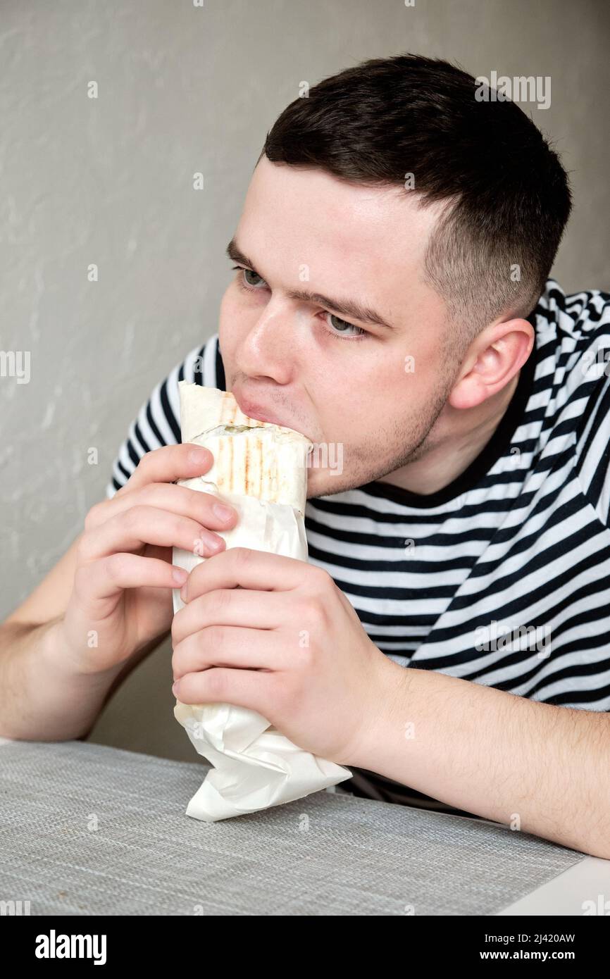 Handsome Young Man Eating Kebab. Hungry Man eating fast food indoors ...