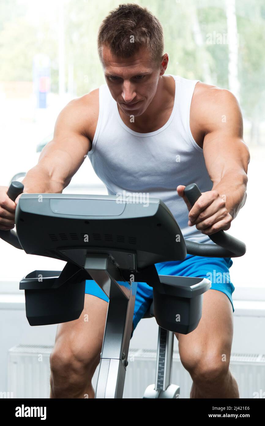 Young muscular man on exercise bike in gym Stock Photo - Alamy
