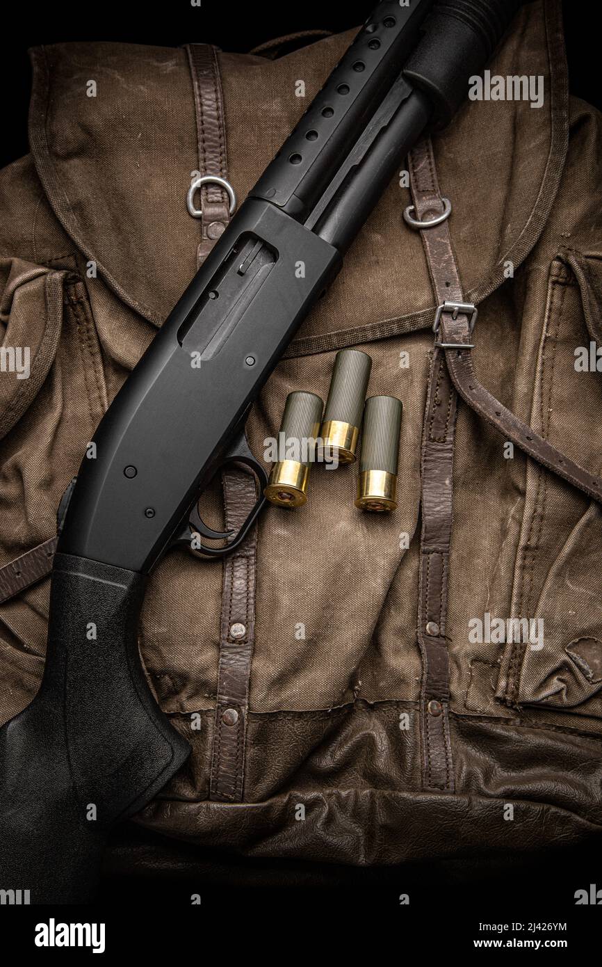 A black 12-gauge pump-action shotgun and ammo are on a canvas backpack ...