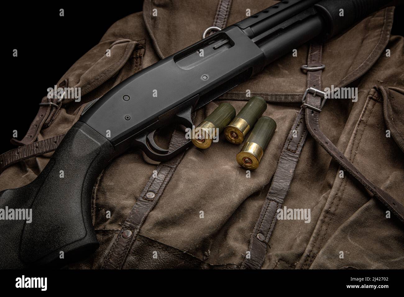 A black 12-gauge pump-action shotgun and ammo are on a canvas backpack ...