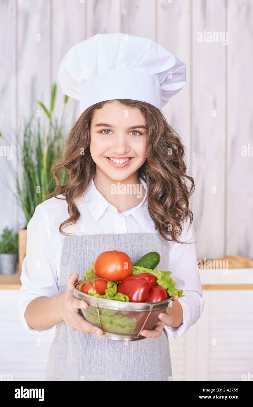 Young girl cooking at kitchen with vegetables. Curly pretty child ...
