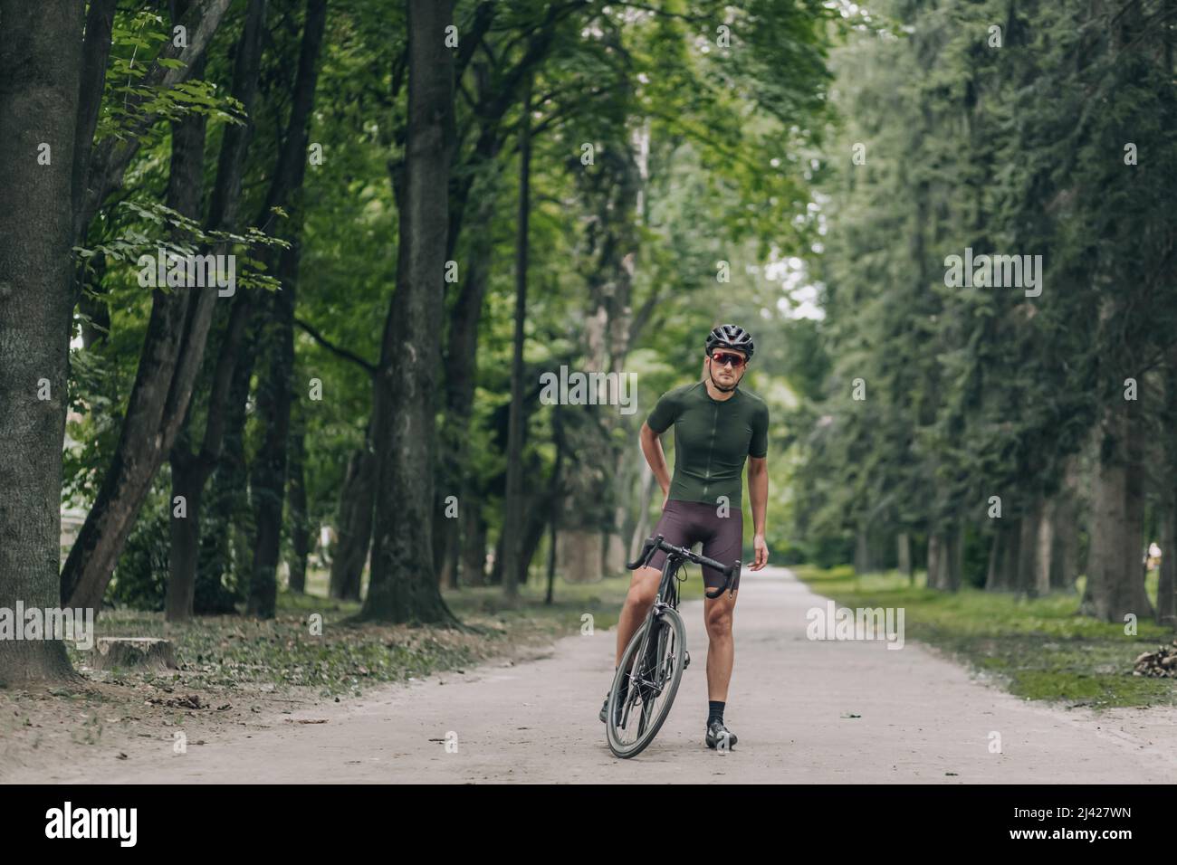 Active young man standing with his bike at green city park. Full length ...