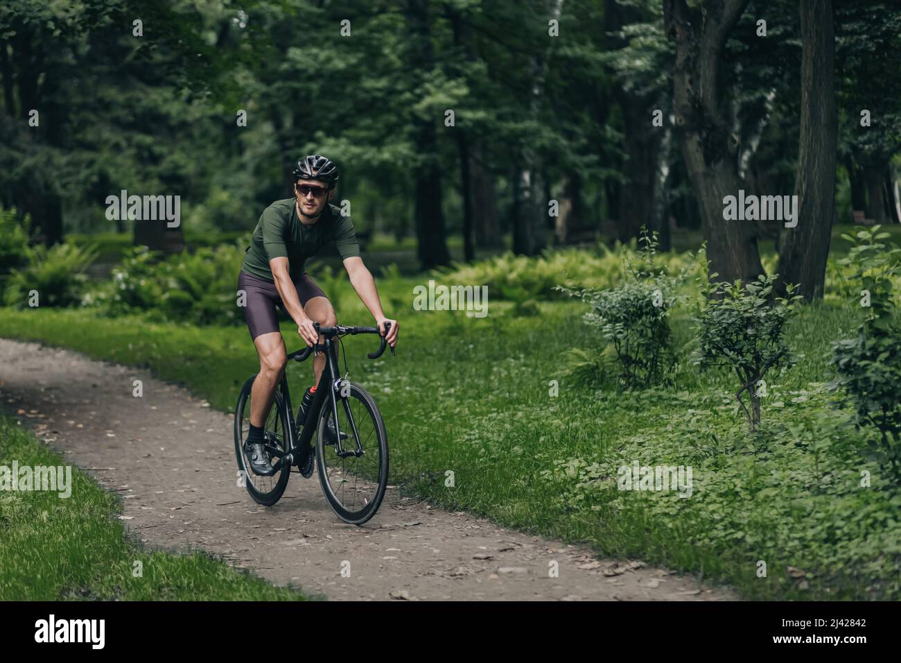 Strong young man having morning ride on black bike at green city park ...