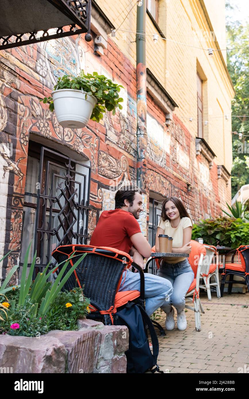 Positive man sitting near girlfriend and paper cups on cafe terrace ...