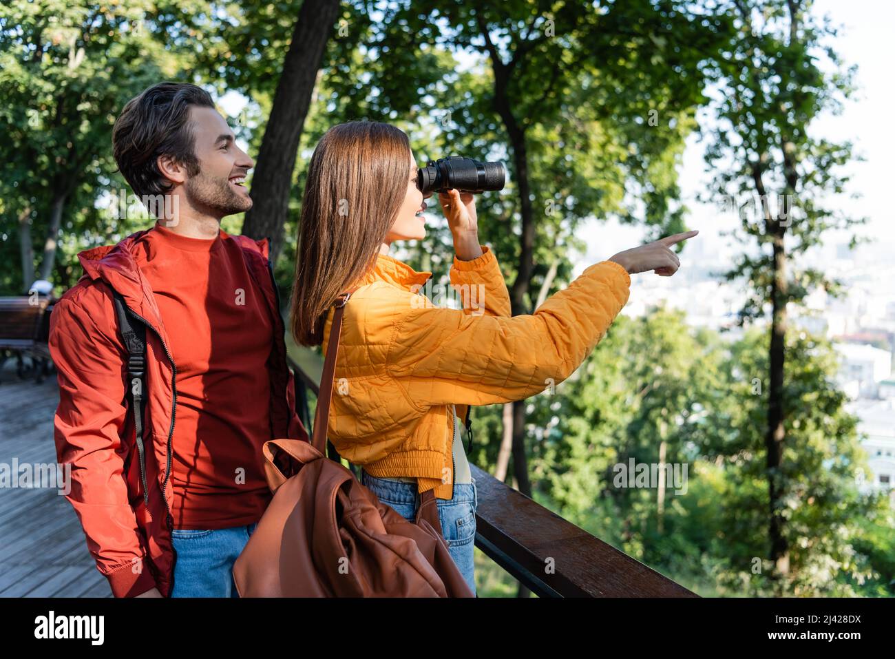 Side view of cheerful traveler looking through binoculars and pointing ...