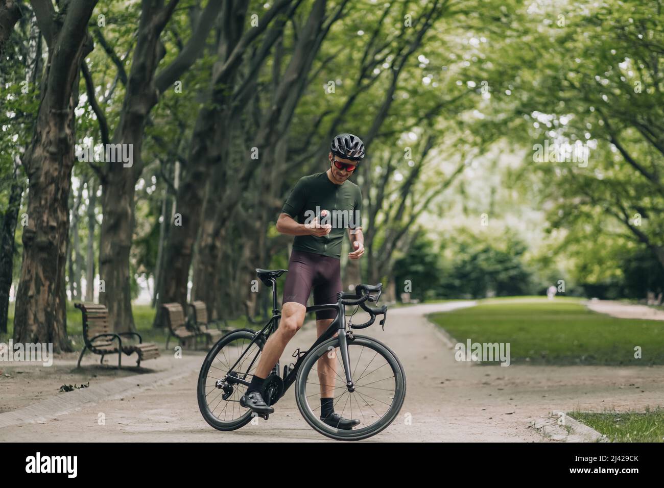 Full length portrait of tired cyclist sitting on black bike and holding ...