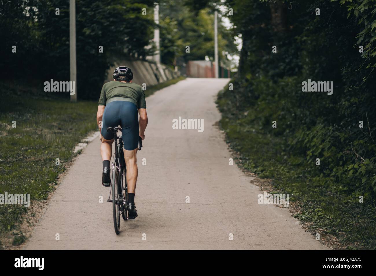 Back view of muscular man in activewear and safety helmet biking alone ...