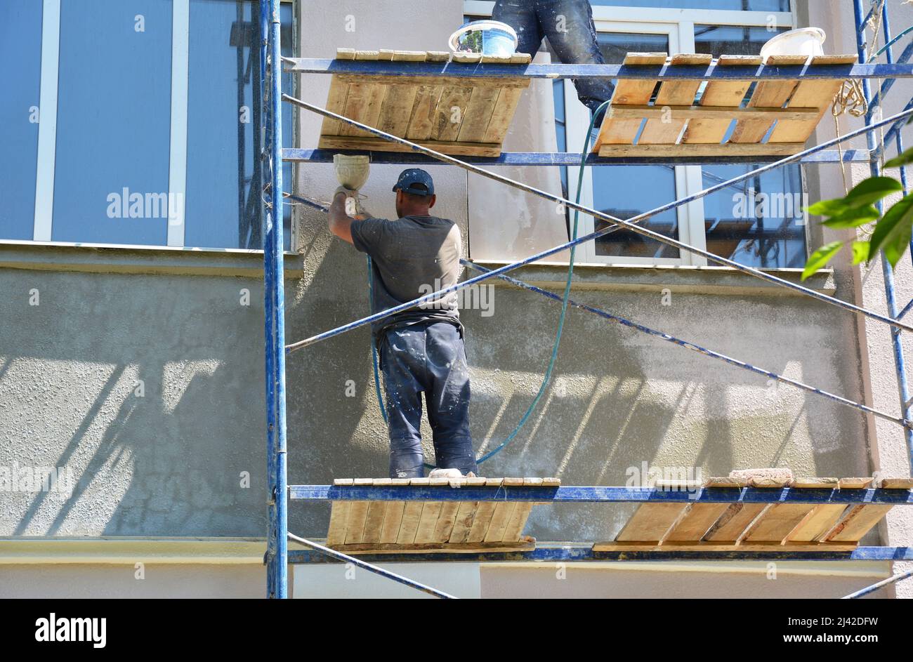 A building contractor is applying stucco on the facade of a house using ...