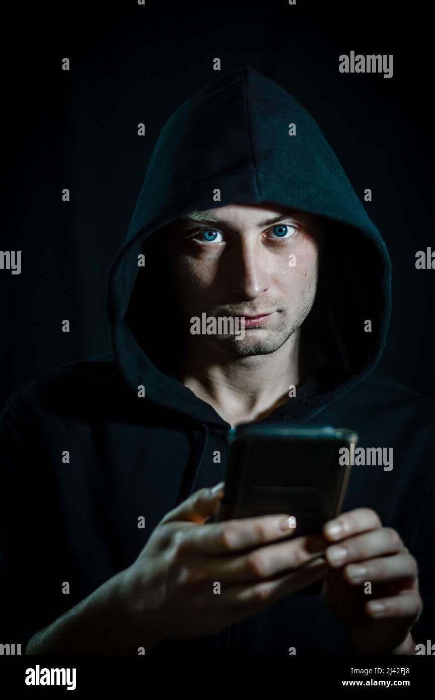 Portrait of a young hooded man who is using a smarphone and looking at ...