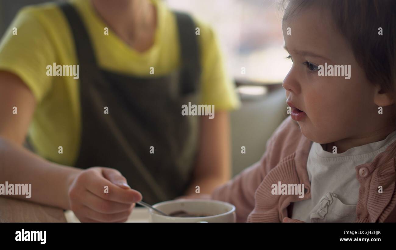 Closeup mom feed young baby in white feeding up high chair, kid is ...