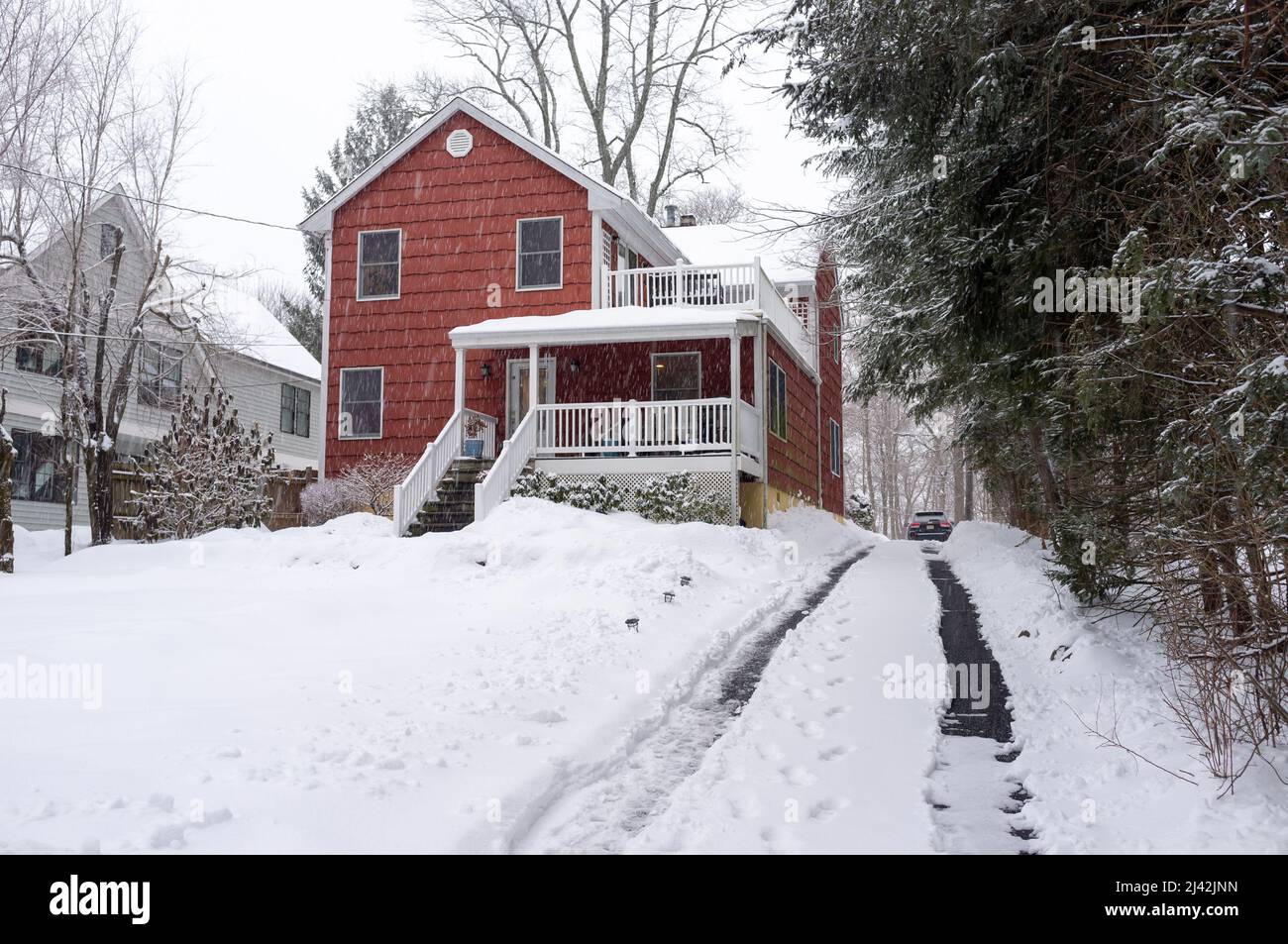 red suburban house with front yard and driveway covered with snow after ...