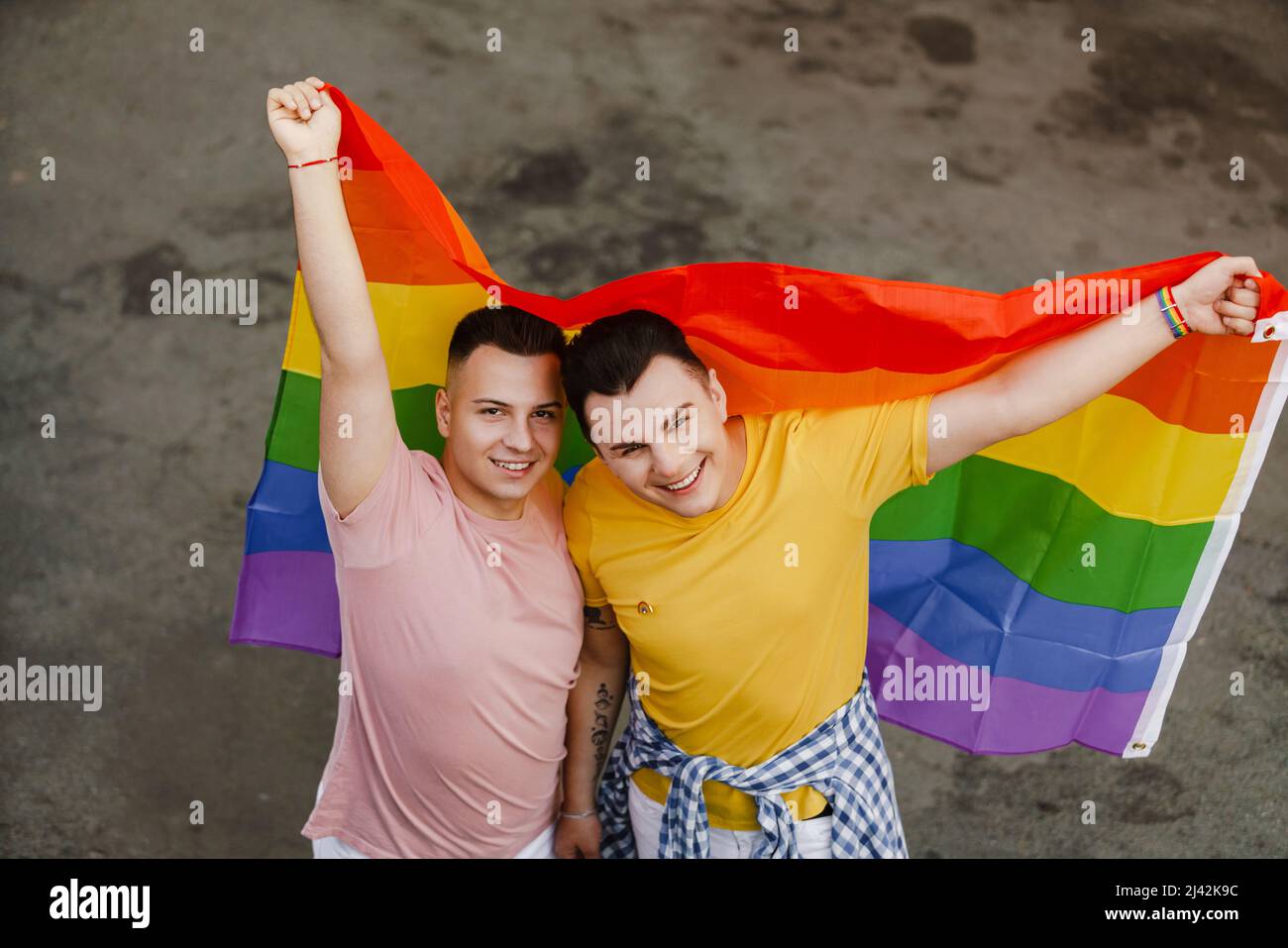 Young gay couple smiling and holding rainbow flag during pride parade ...