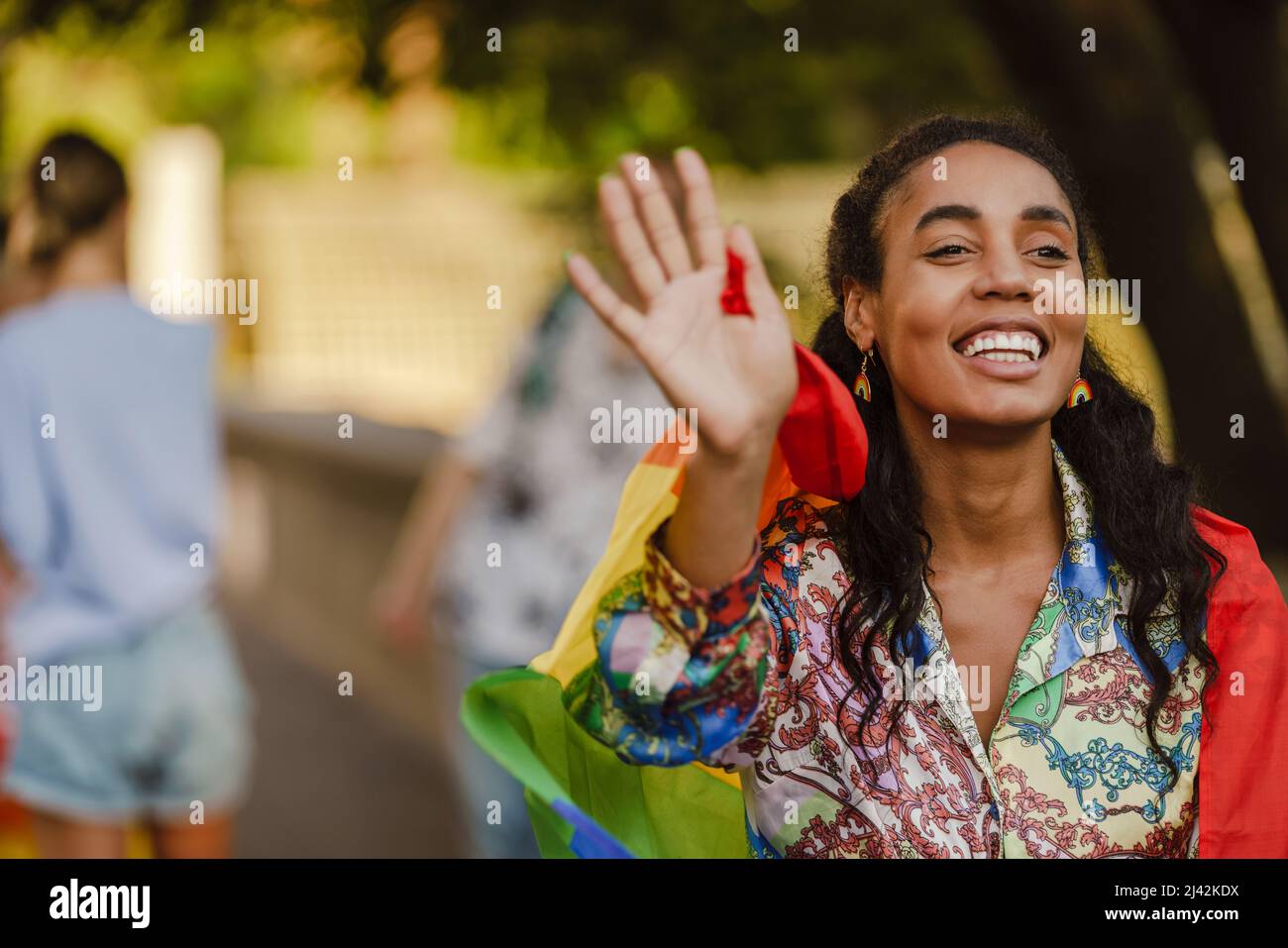Black woman smiling and holding rainbow flag during pride parade at ...