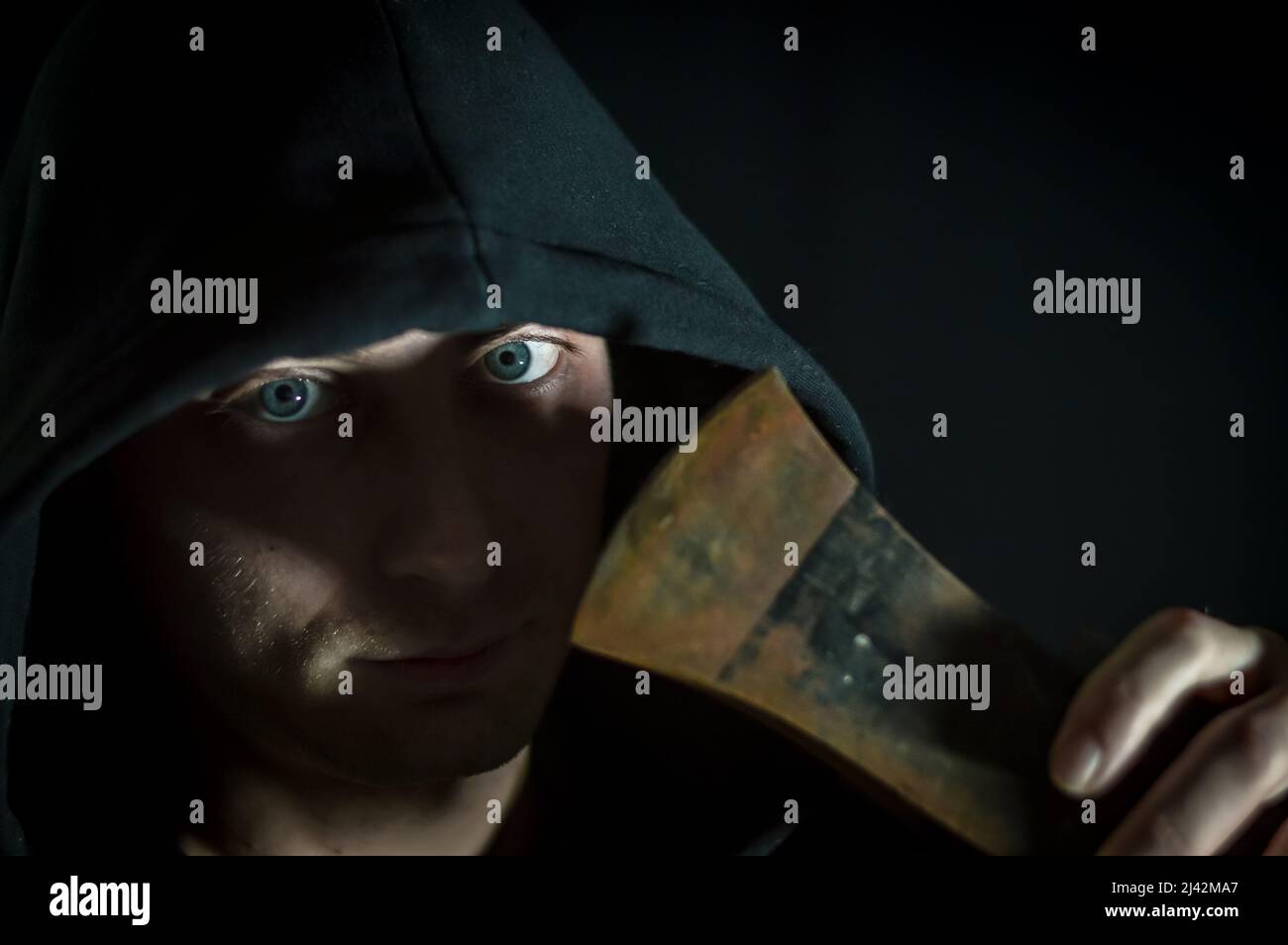 Portrait of a young hooded man with blue eyes who with an ax in his ...
