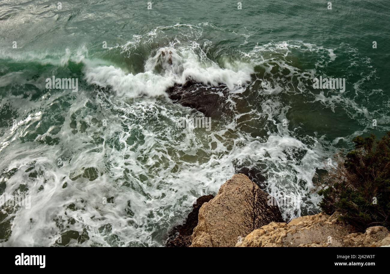 Abstract seascape movement of waves breaking against a protruding rock ...