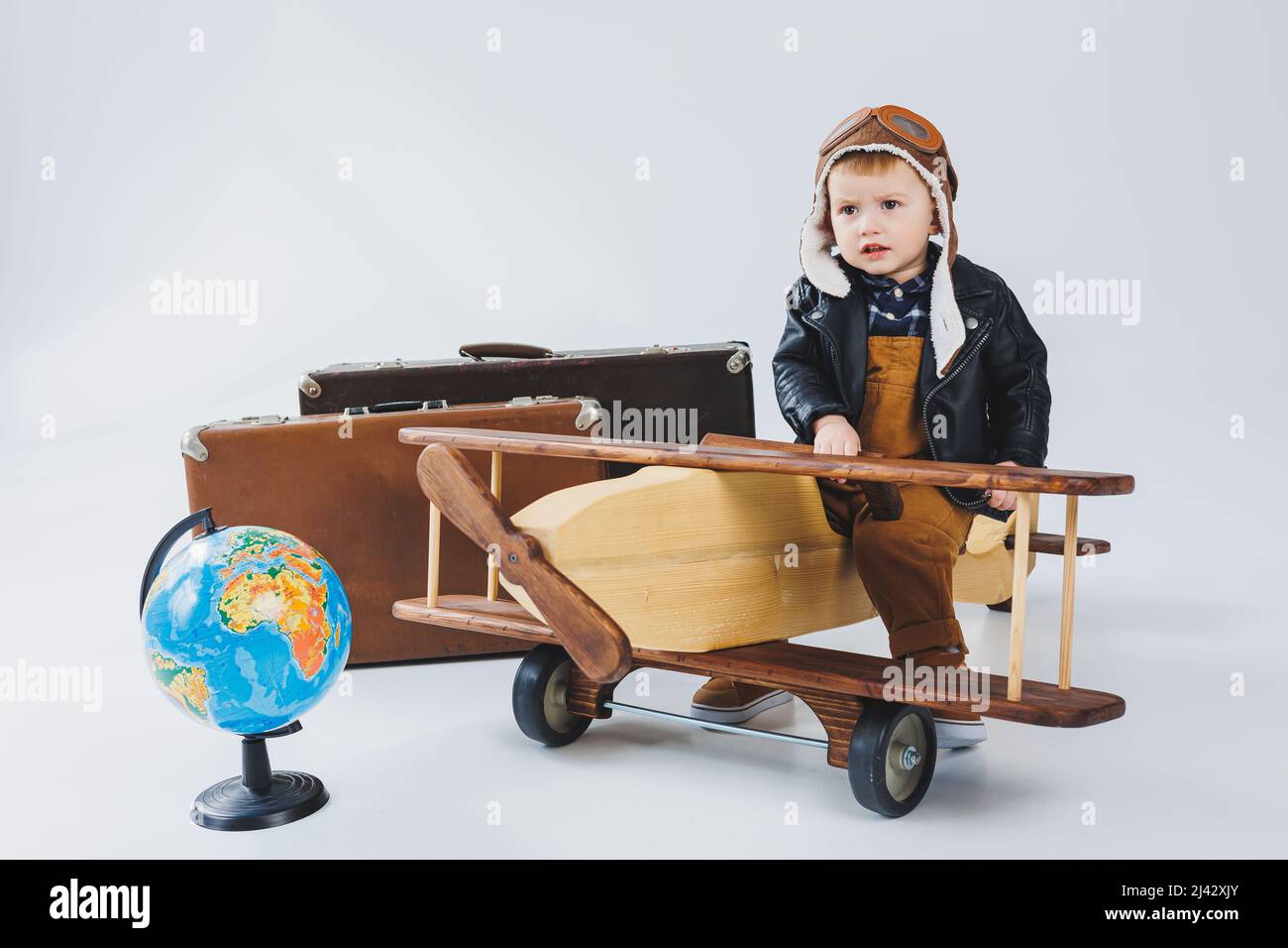 A boy in a leather jacket and a pilot's hat, a wooden plane, a globe ...