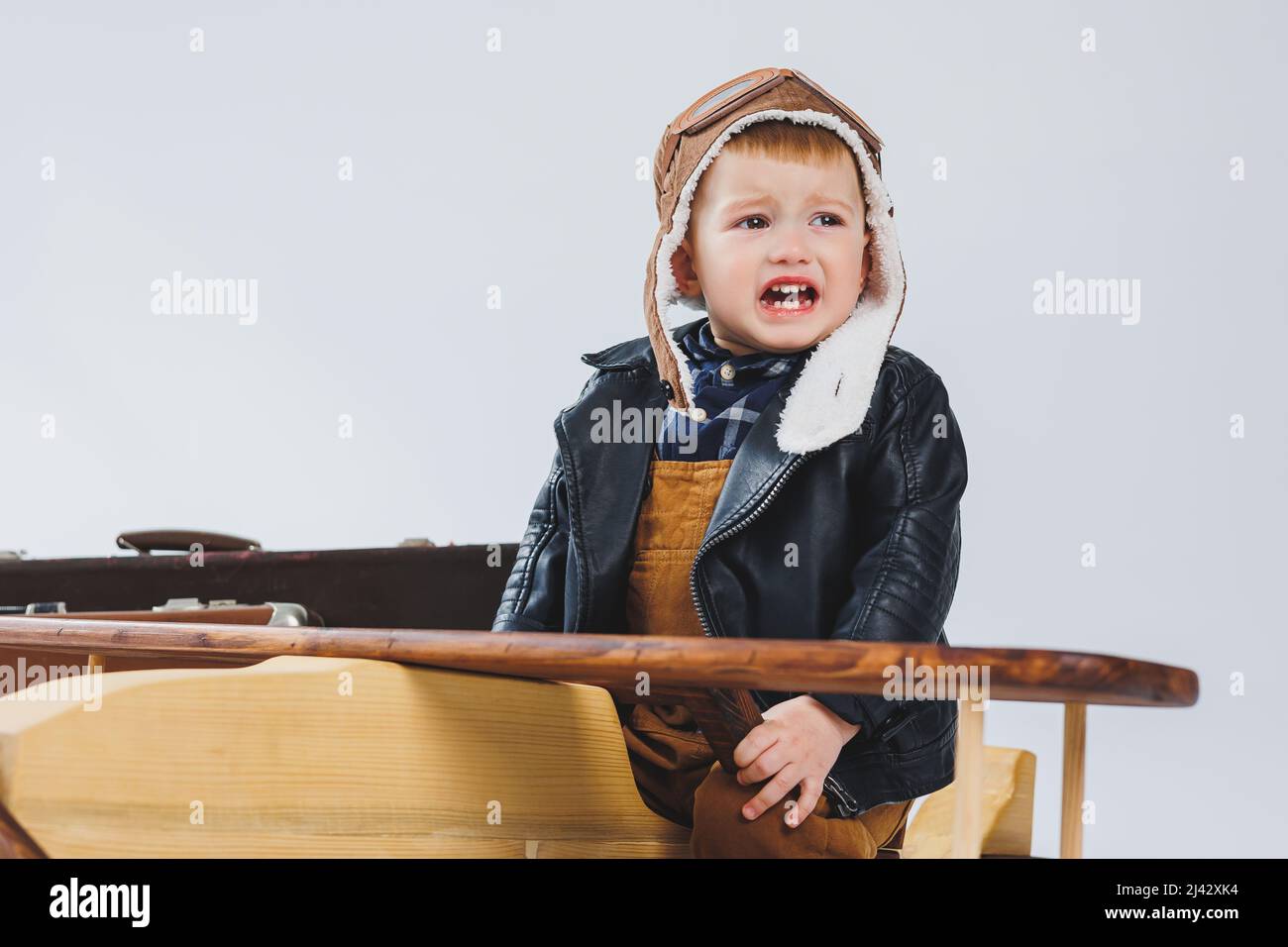 The boy is crying in a leather jacket and a pilot's hat, a wooden plane ...