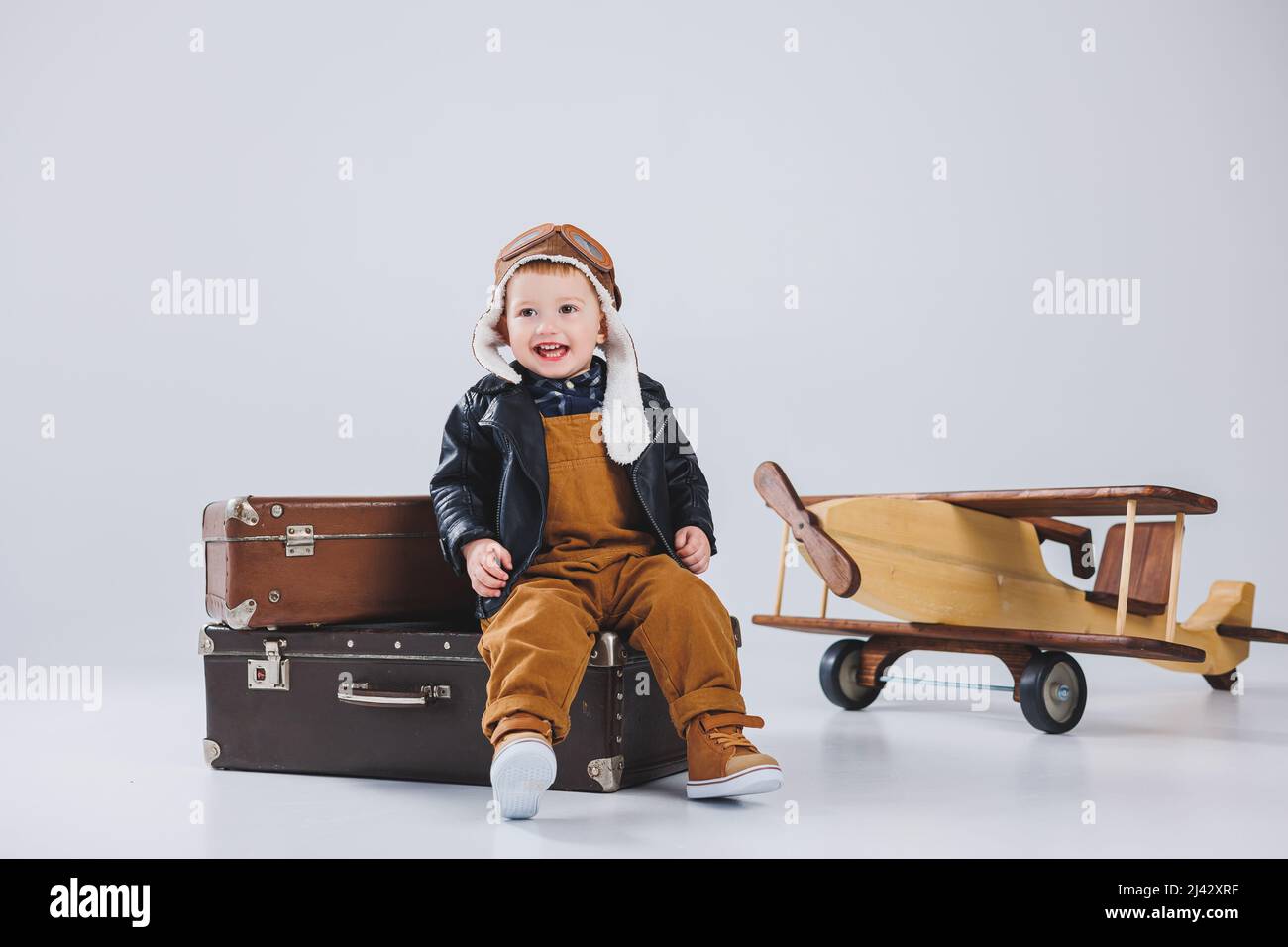 A happy boy in a helmet and a pilot's jacket stands near a wooden plane ...