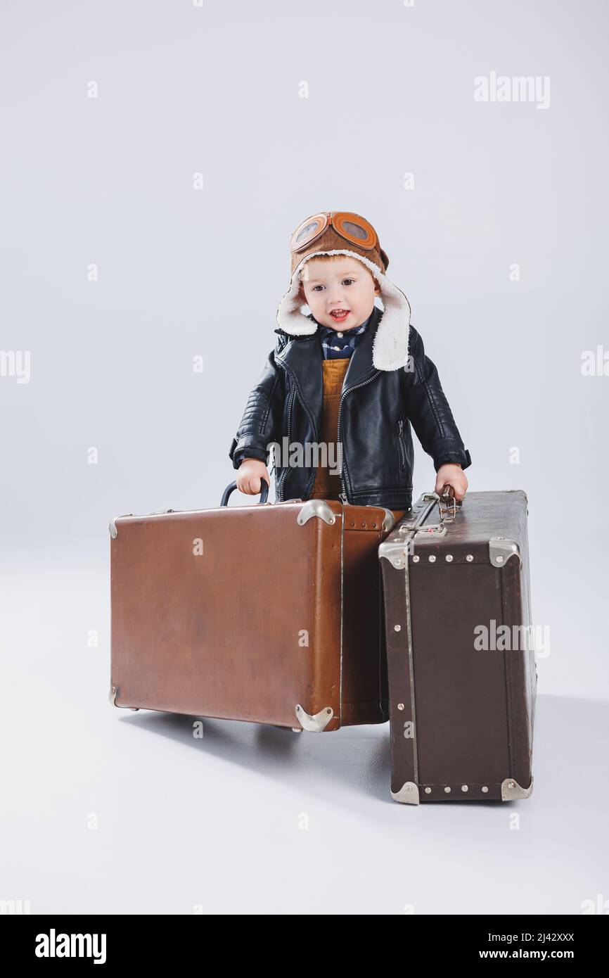 A happy boy in a helmet and a pilot's jacket carries a brown suitcase ...