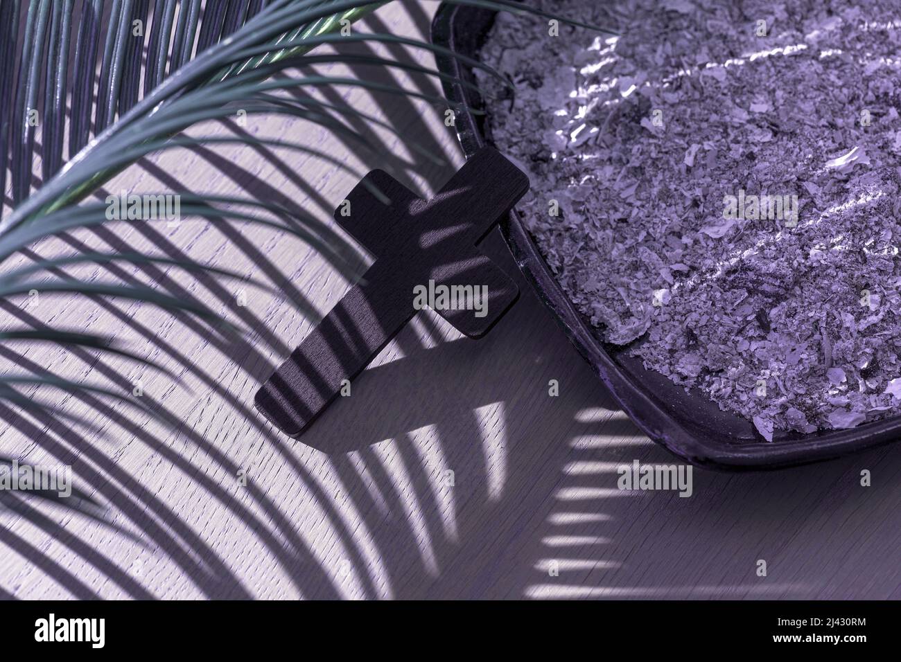 A Christian cross with palm leaf shadow on ashes background. Lent ...