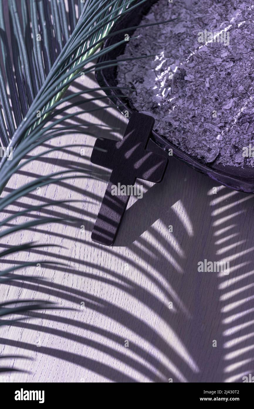 A Christian cross with palm leaf shadow on ashes background. Lent ...