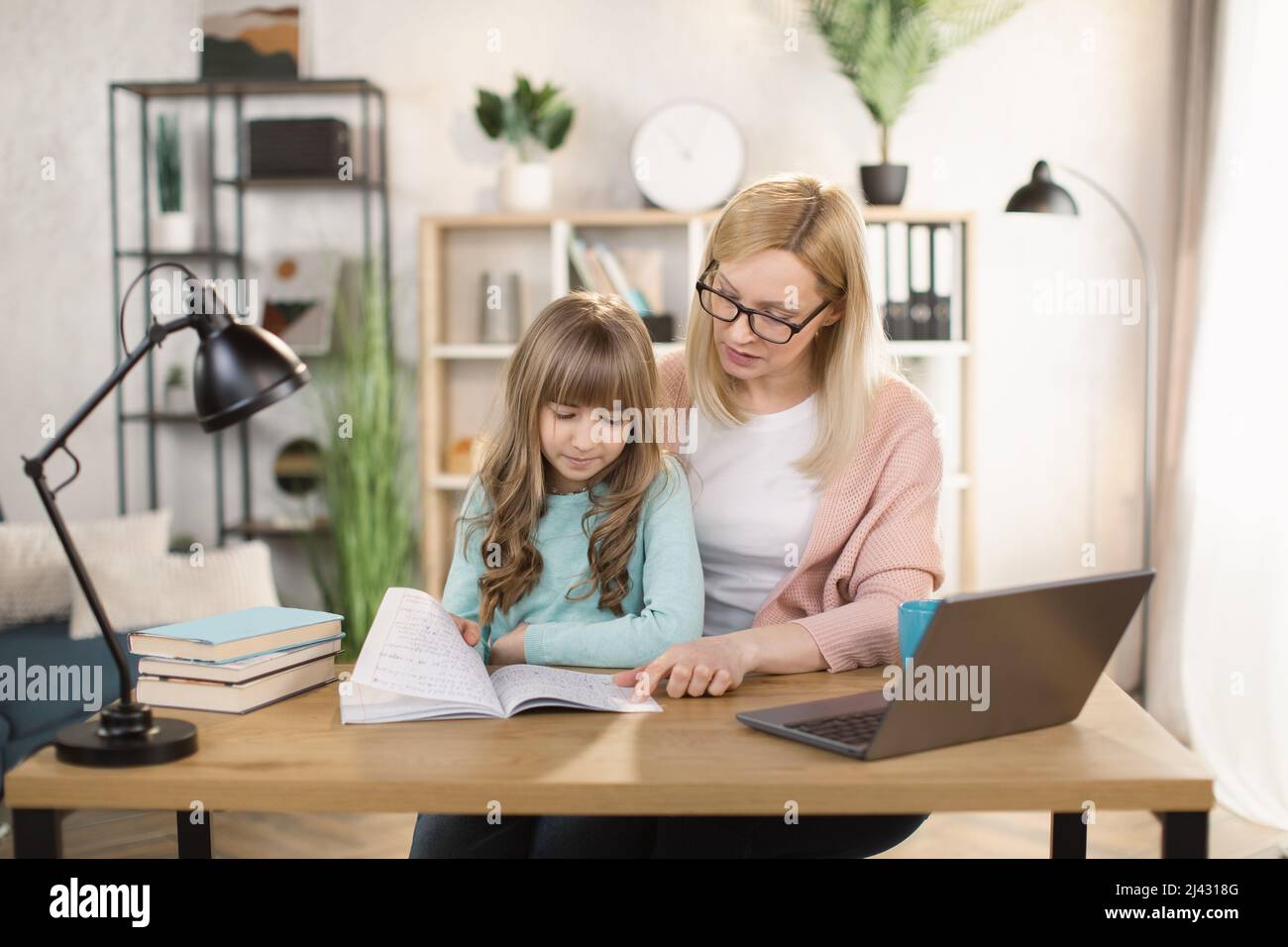 Young caucasian mother helping daughter remote studying at home ...