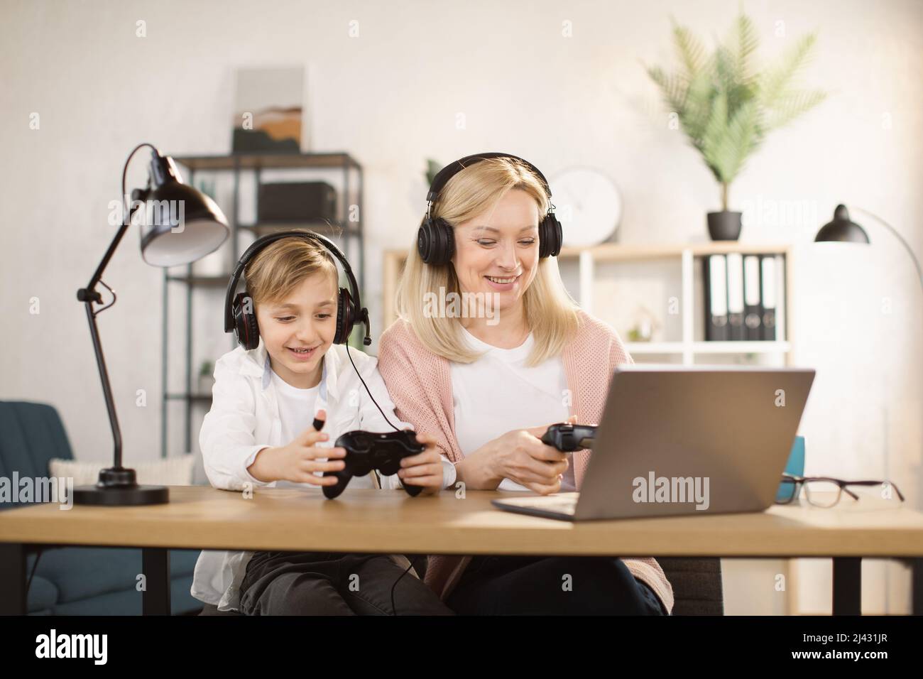 Child son and mother playing video games using joysticks on laptop ...