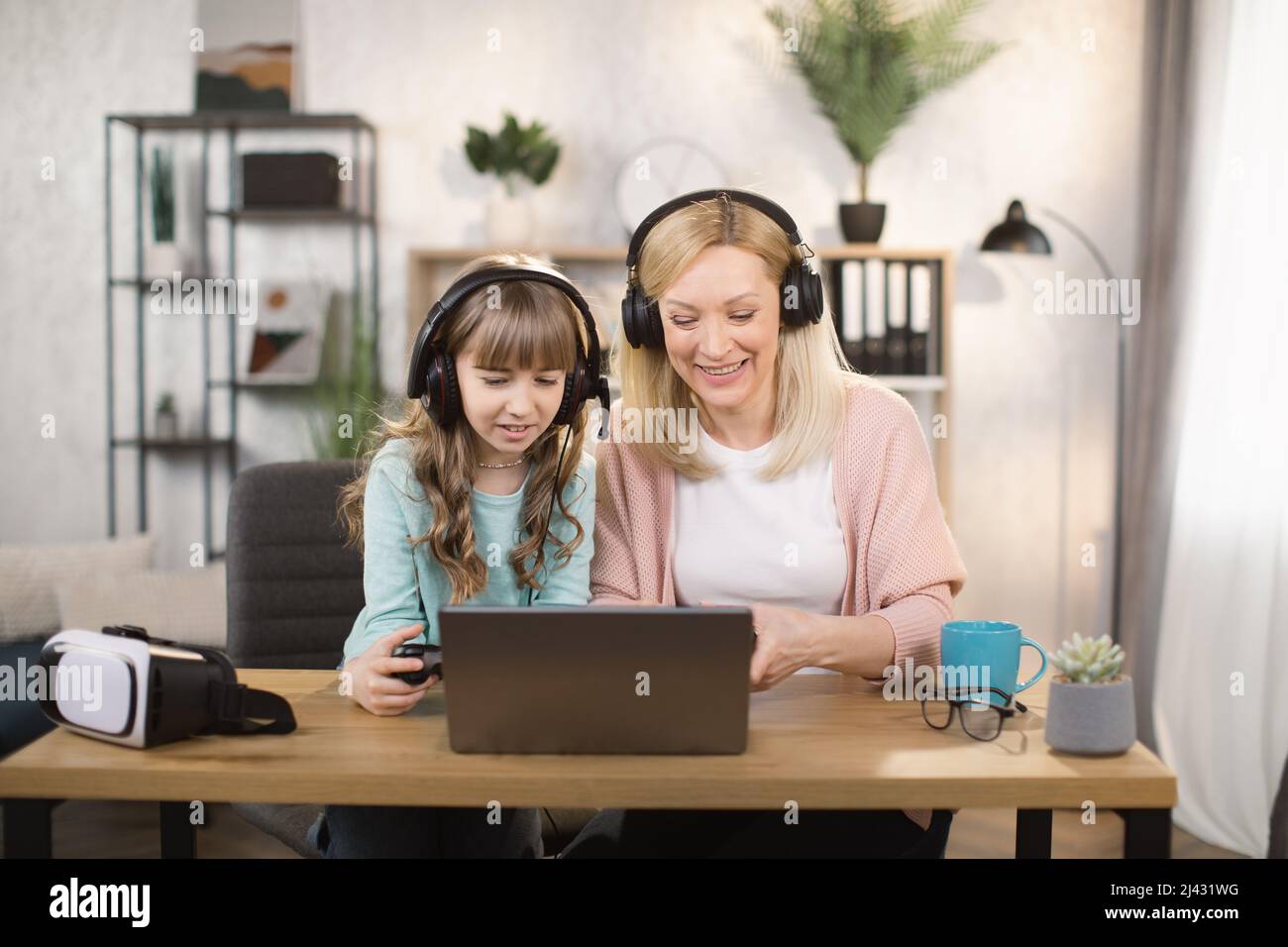 Child daughter and mother playing video games using joysticks on laptop ...