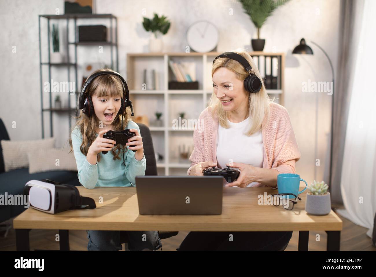 Happy woman and daughter play video games sitting at a table in the ...