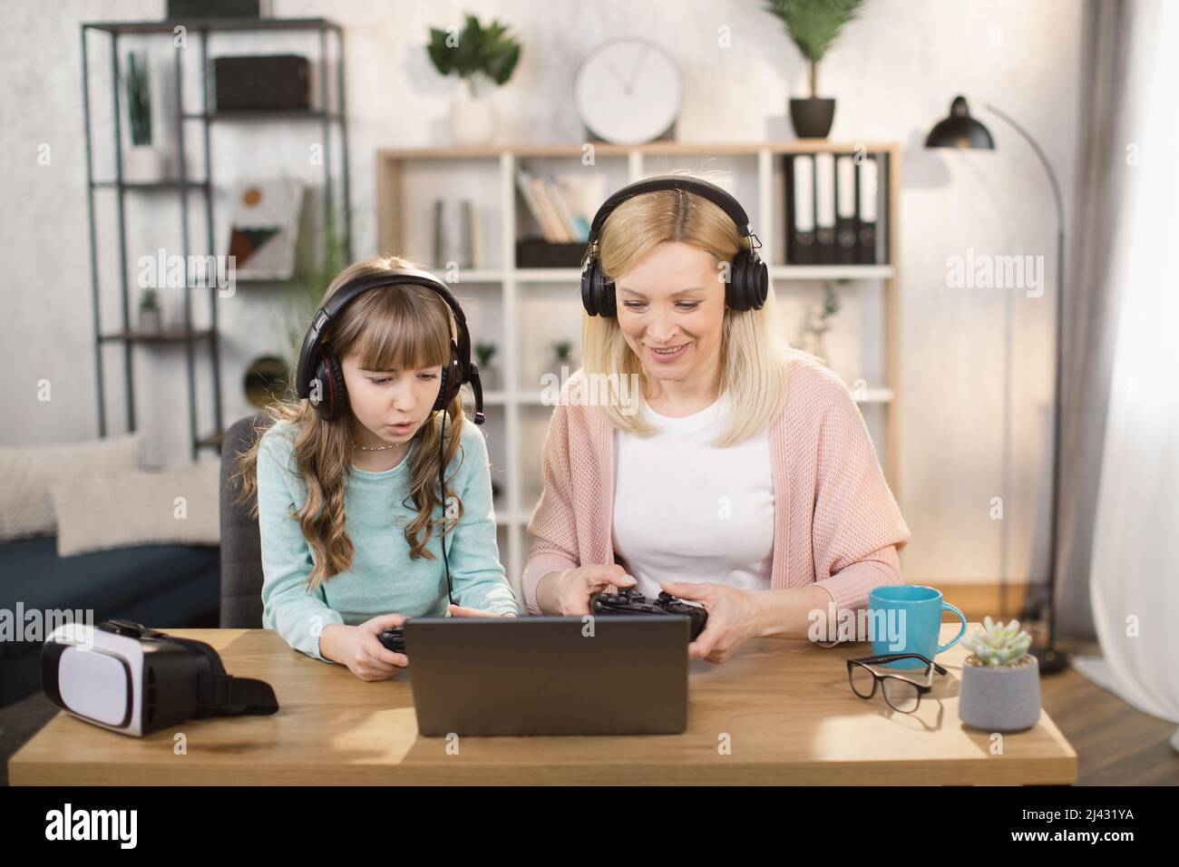 Child daughter and mother playing video games using joysticks on laptop ...