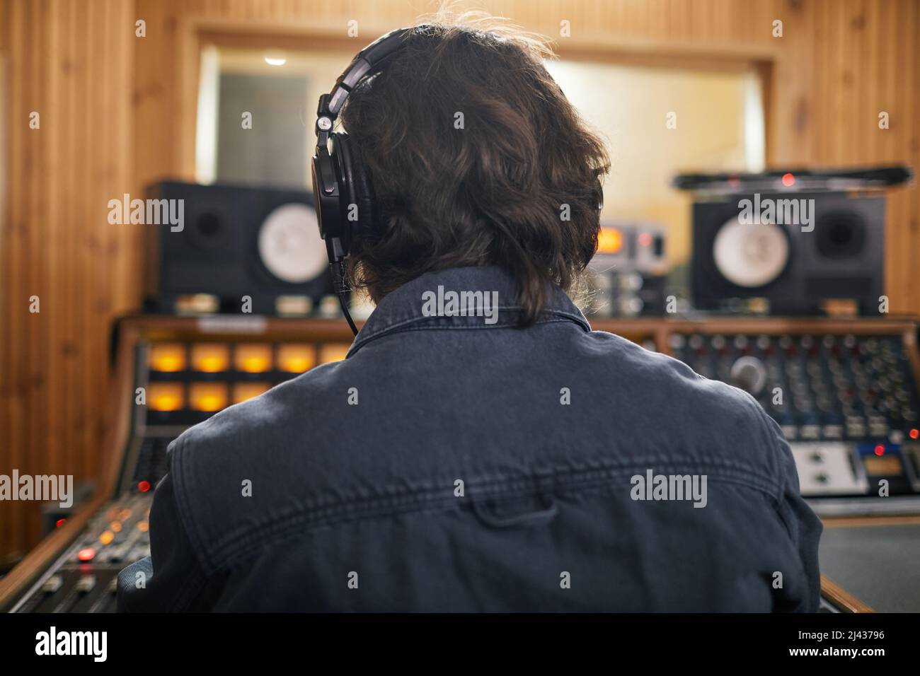 Back view of man wearing headphones at audio workstation in ...