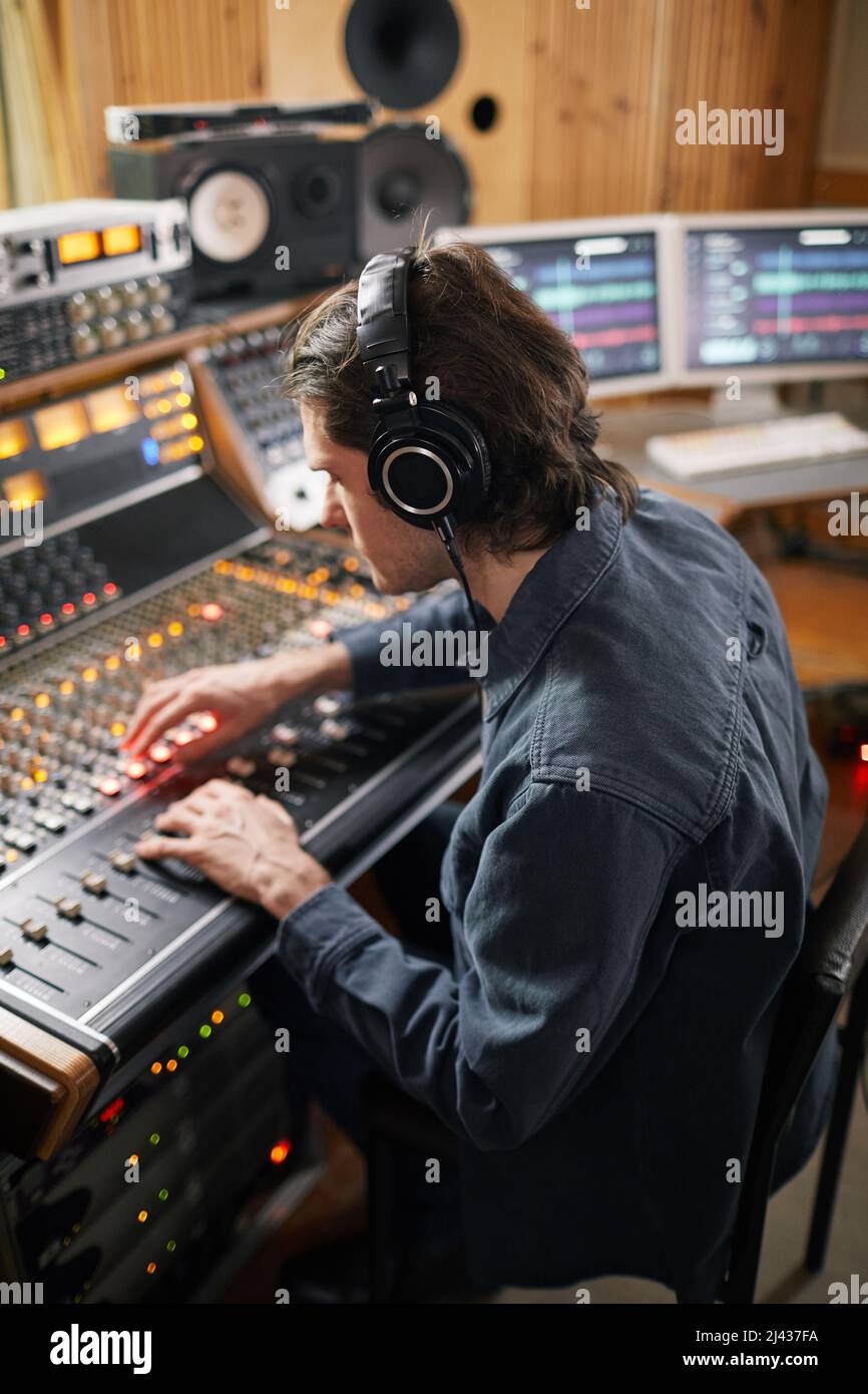 Side view portrait of man wearing headphones at audio workstation in ...