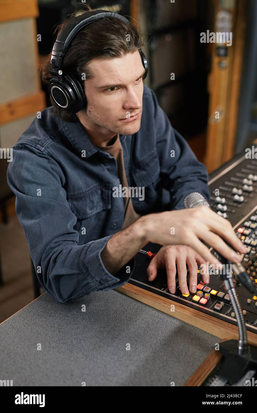 Vertical portrait of young man wearing headphones at audio workstation ...