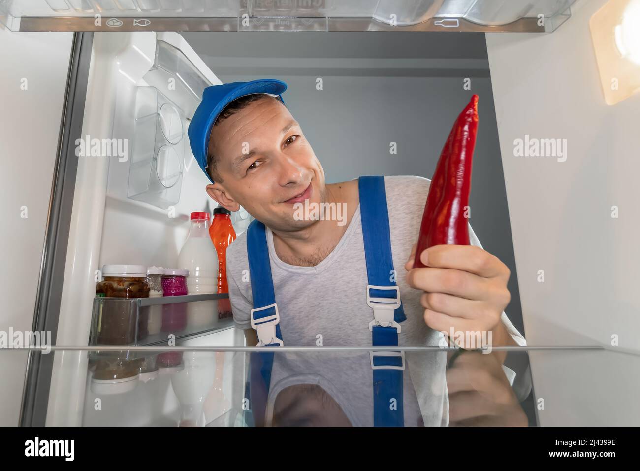 Male repairman in uniform smiles and holds a red pepper from the ...