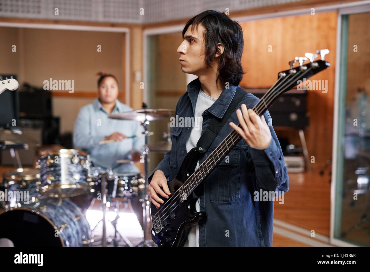 Side view portrait of young man playing bass guitar while recording new ...