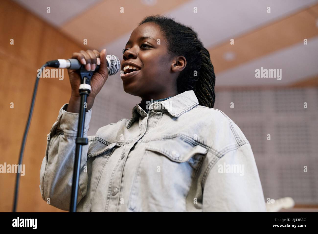 Low angle portrait of young black woman singing to microphone while ...